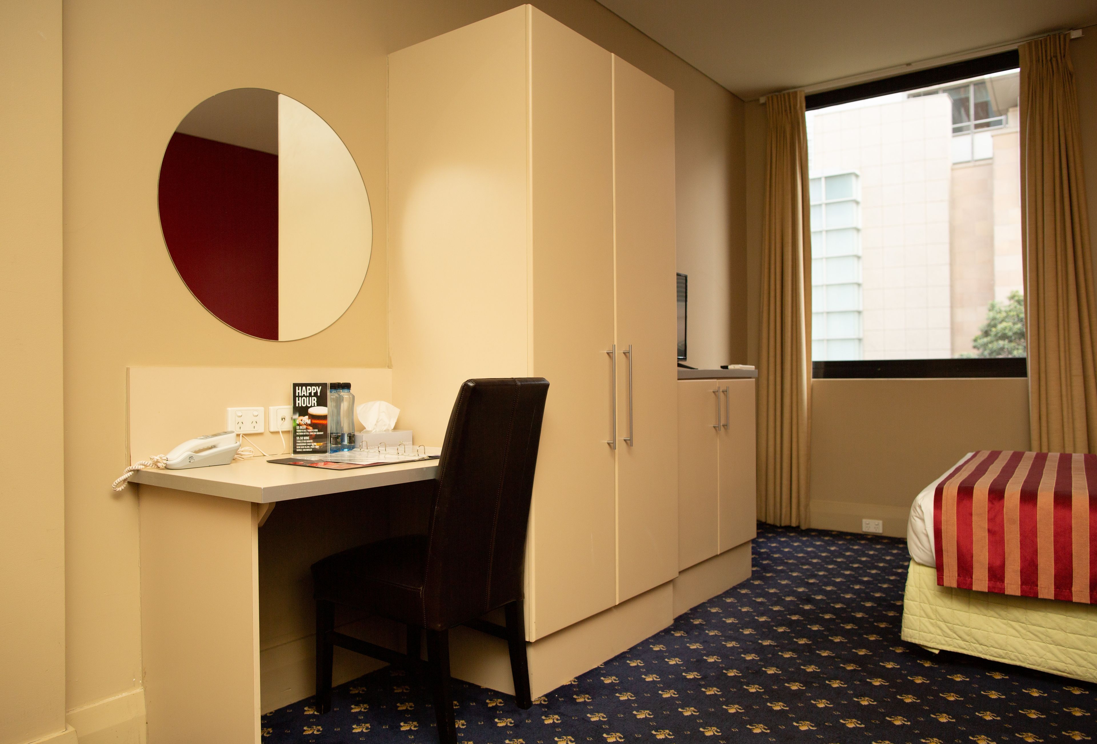 Quarto de hotel com escrivaninha, cadeira, cama e um espelho grande.