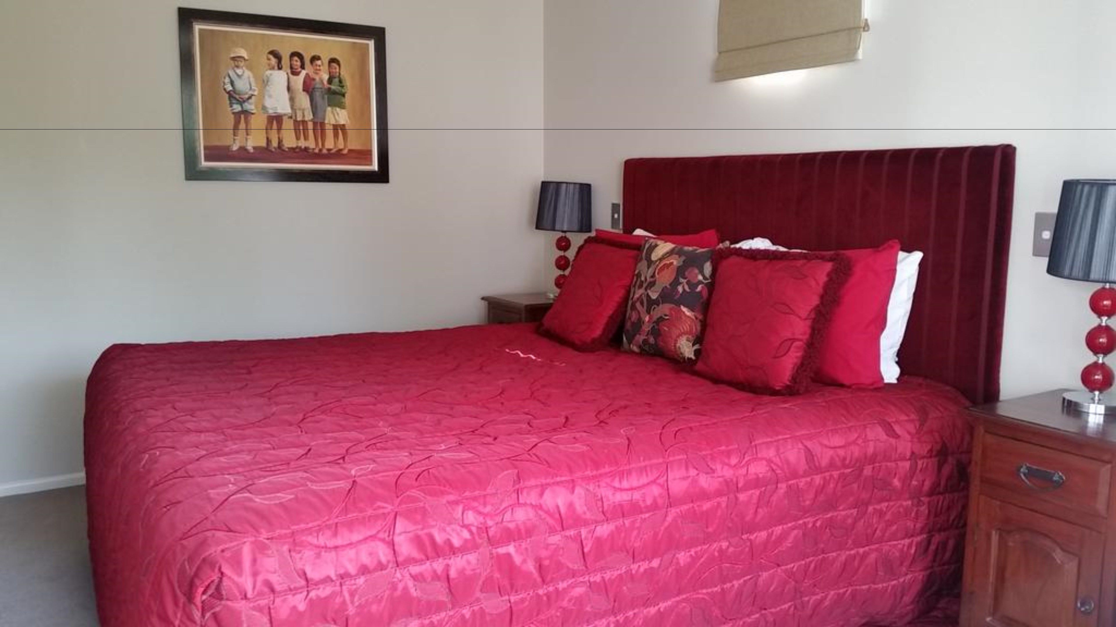 Uma cama com colcha vermelha, duas luminárias de cabeceira e uma mesa de cabeceira com abajur vermelho.