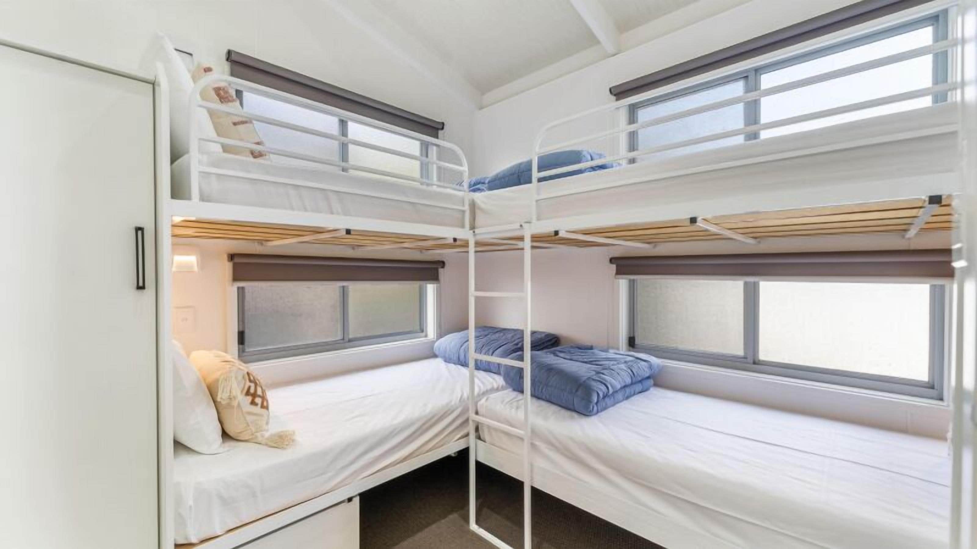 Um quarto compacto de motorhome com duas beliches, uma janela pequena e uma porta.
