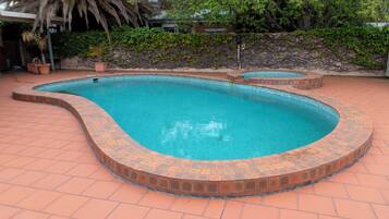 Piscina com borda curva, rodeada por um deck revestido com azulejos.