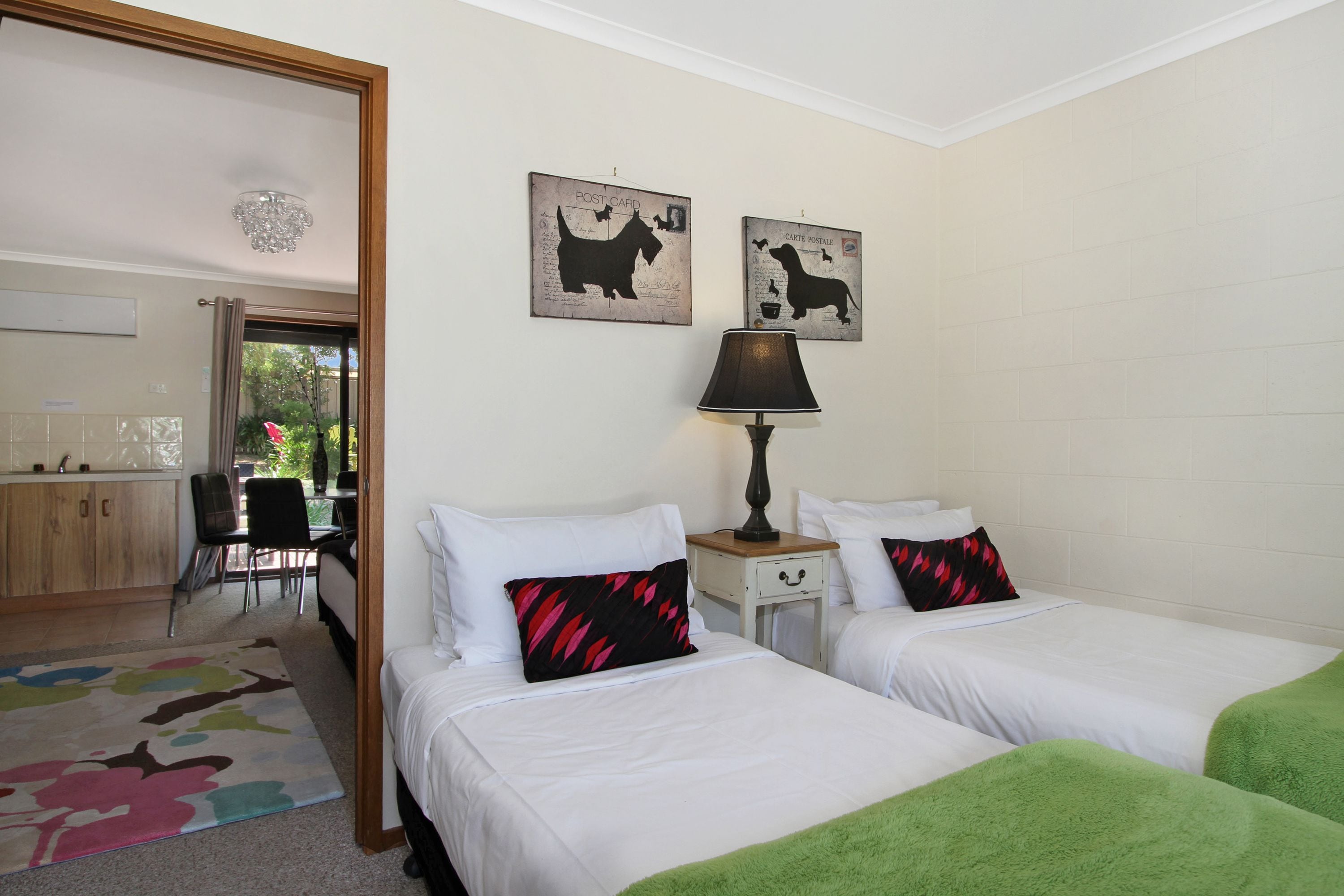 Quarto de hotel com duas camas, uma escrivaninha, uma cadeira, um abajur e vista para o exterior.