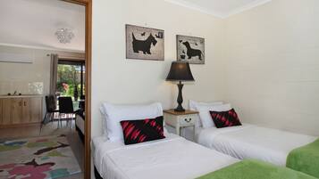 Quarto de hotel com duas camas, uma escrivaninha, uma cadeira, um abajur e vista para o exterior.