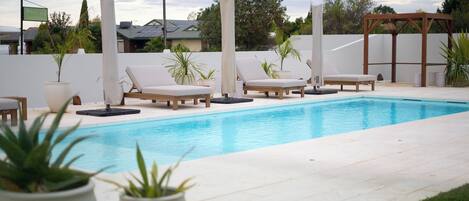 Uma piscina com espreguiçadeiras, plantas em vasos e um pérgola.