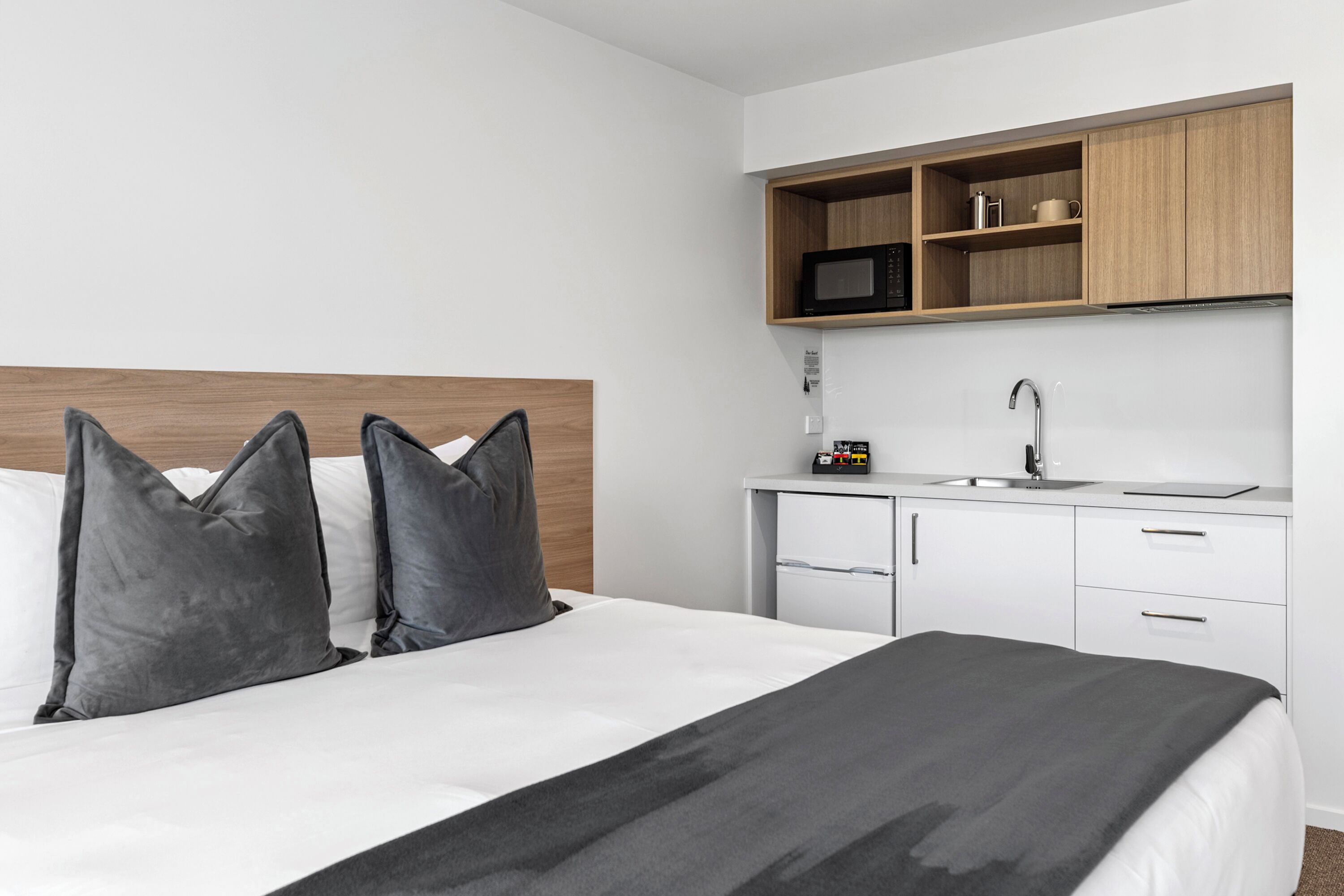 Quarto de hotel com cama, mesa de cabeceira, micro-ondas, pia e armário.