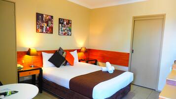 Quarto de hotel com uma cama, duas mesas de cabeceira, uma cadeira, uma mesinha e obras de arte nas paredes.