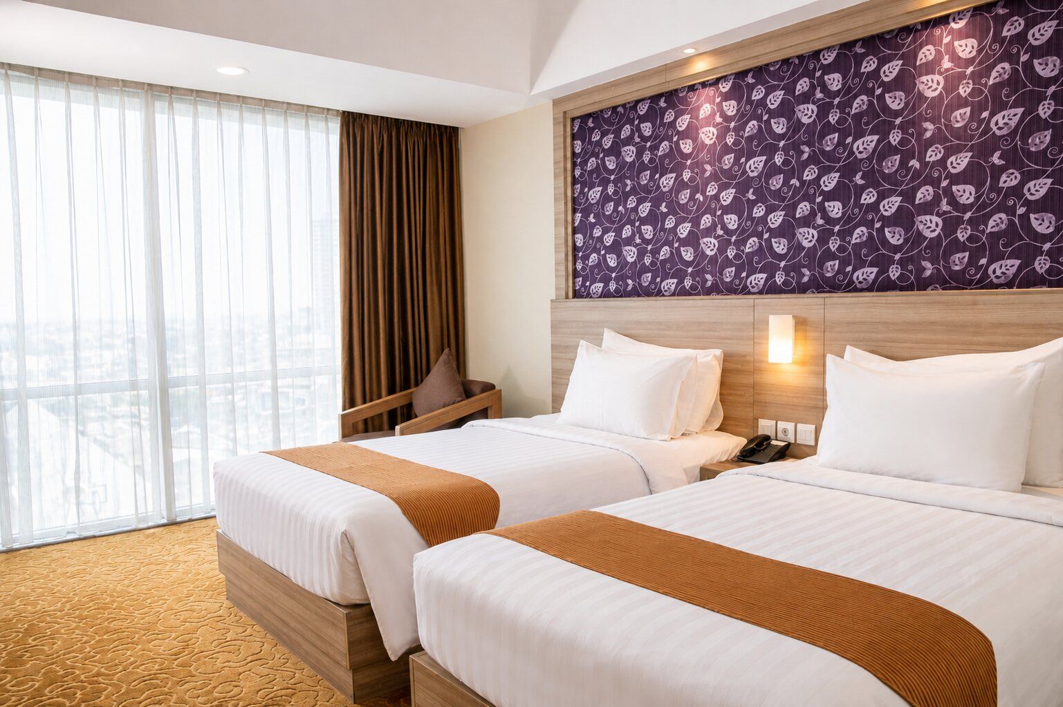 Quarto de hotel com duas camas, uma janela grande com cortinas, cabeceira estampada e vista para a cidade.