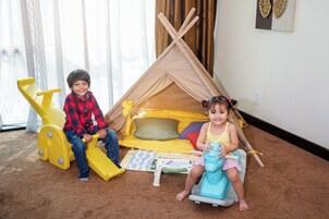 Duas crianças brincando em um quarto com uma tenda de brincadeira, um escorregador amarelo e um cavalo de brinquedo.