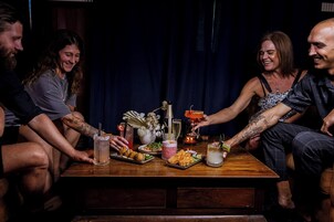 Um grupo de pessoas sentado ao redor de uma mesa de madeira com diversos alimentos e bebidas.