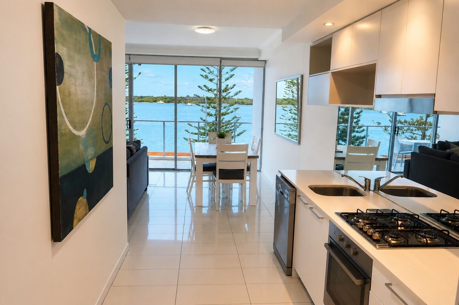 Uma cozinha moderna com vista para o mar, uma sala de jantar com mesa e cadeiras, e um quadro grande na parede.