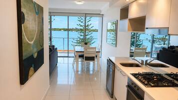 Uma cozinha moderna com vista para o mar, uma sala de jantar com mesa e cadeiras, e um quadro grande na parede.