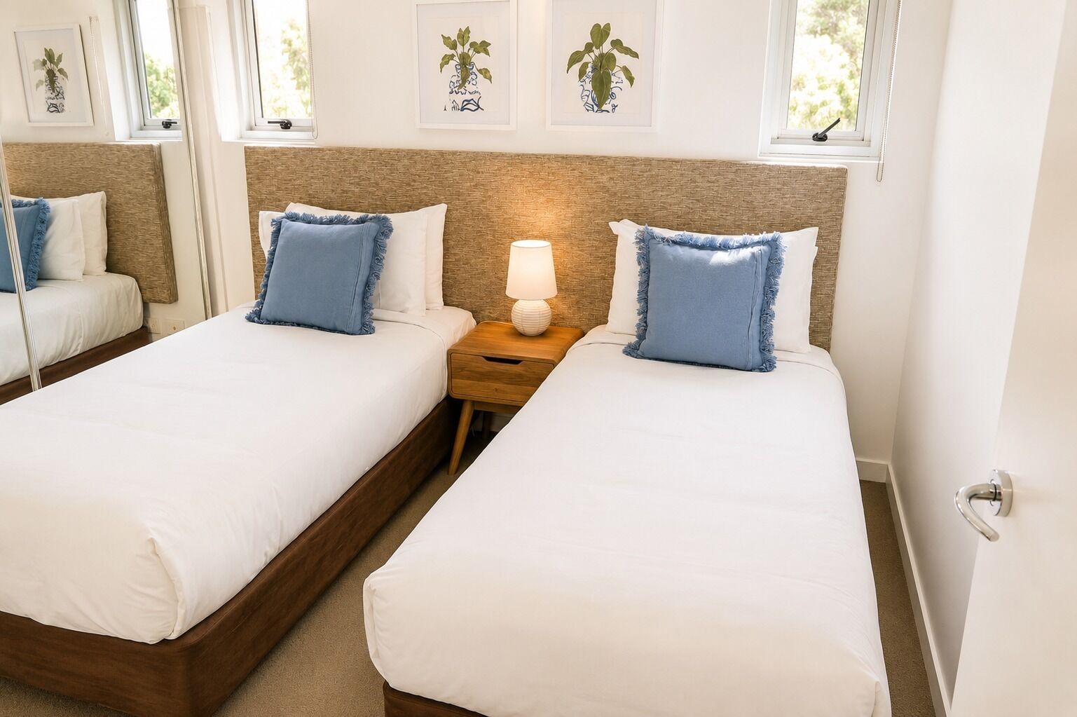 Quarto de hotel com duas camas, uma mesa de cabeceira com abajur e quadros nas paredes.