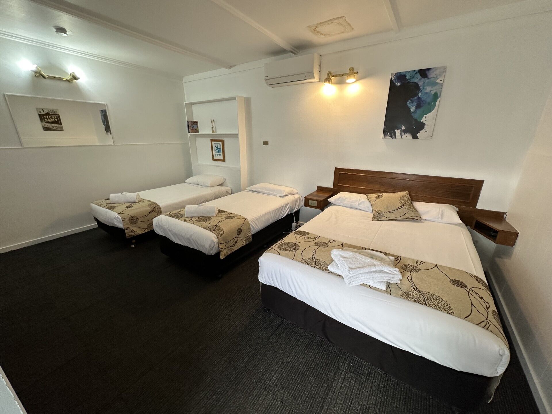 Quarto de hotel com três camas de solteiro, uma cama de casal e uma mesinha.