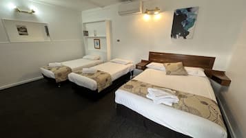 Quarto de hotel com três camas de solteiro, uma cama de casal e uma mesinha.