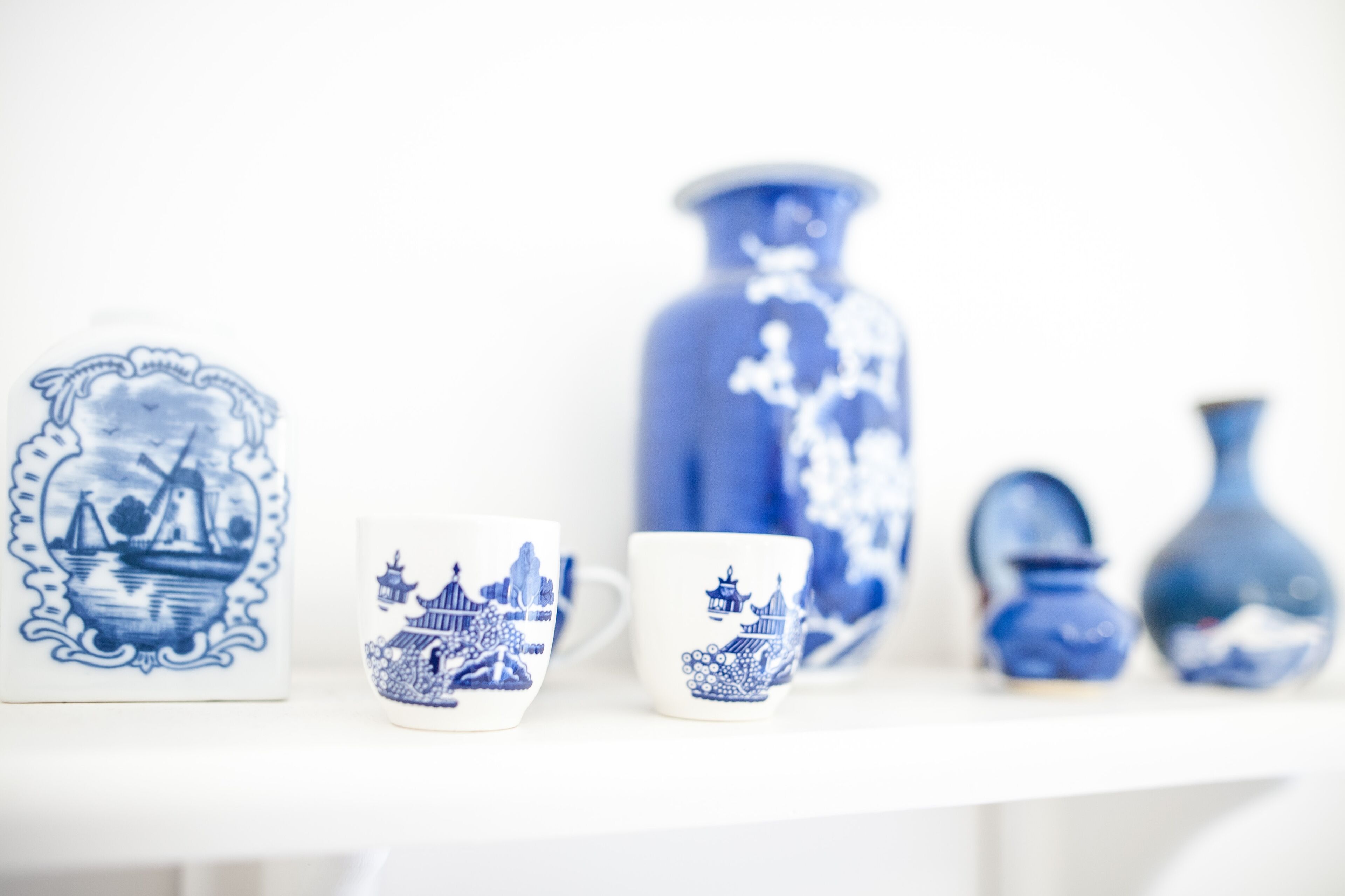 Uma prateleira branca com diversos objetos de cerâmica azul, incluindo um vaso, uma xícara e um prato decorativo.