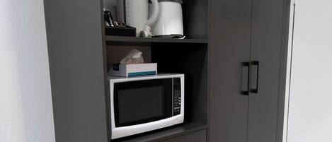 Uma cozinha compacta equipada com micro-ondas, cafeteira e mini-geladeira.