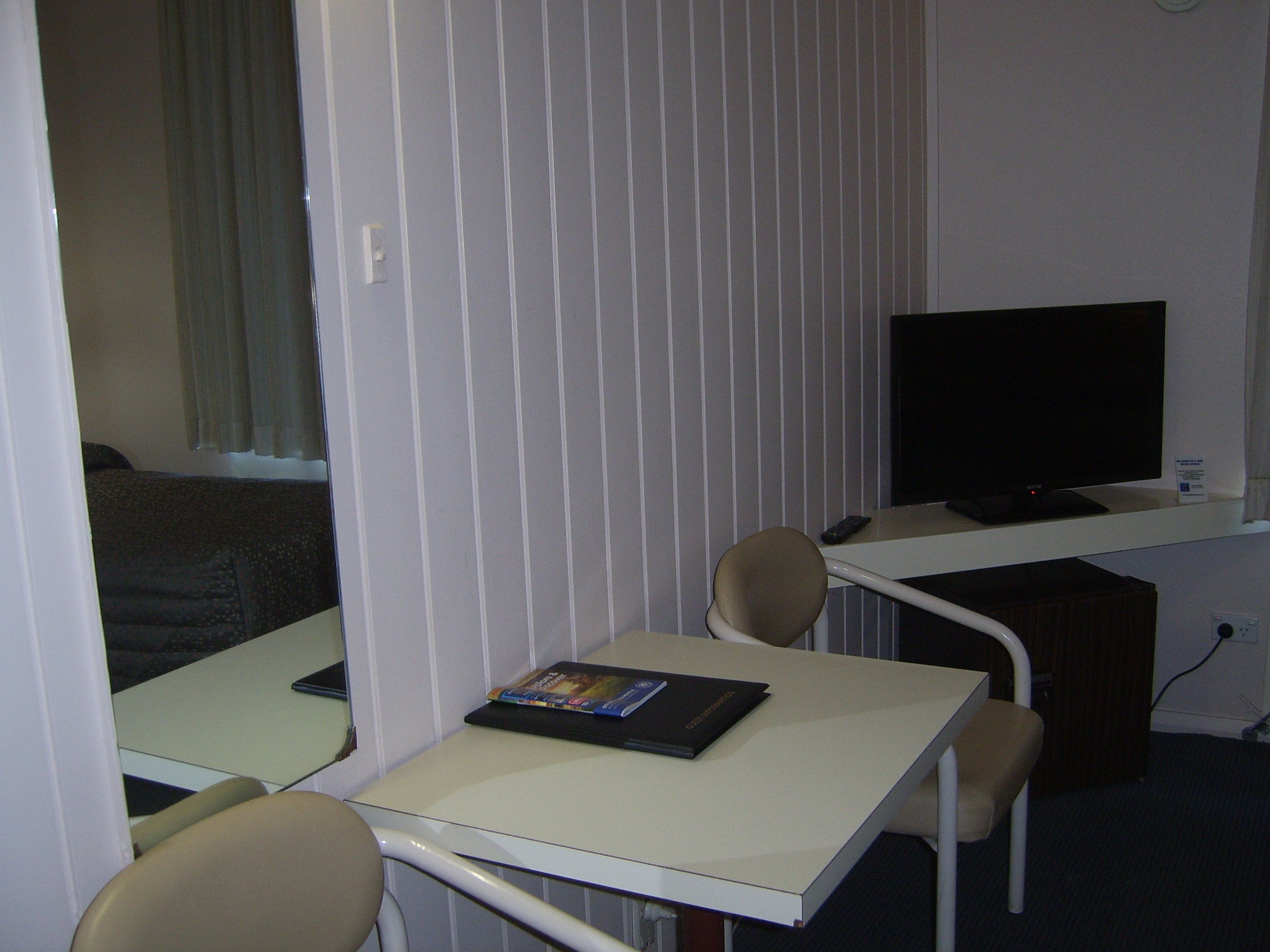 Quarto de hotel pequeno com uma cama de solteiro, uma mesa de escritório com um computador e uma televisão, e uma cadeira.