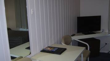 Quarto de hotel pequeno com uma cama de solteiro, uma mesa de escritório com um computador e uma televisão, e uma cadeira.