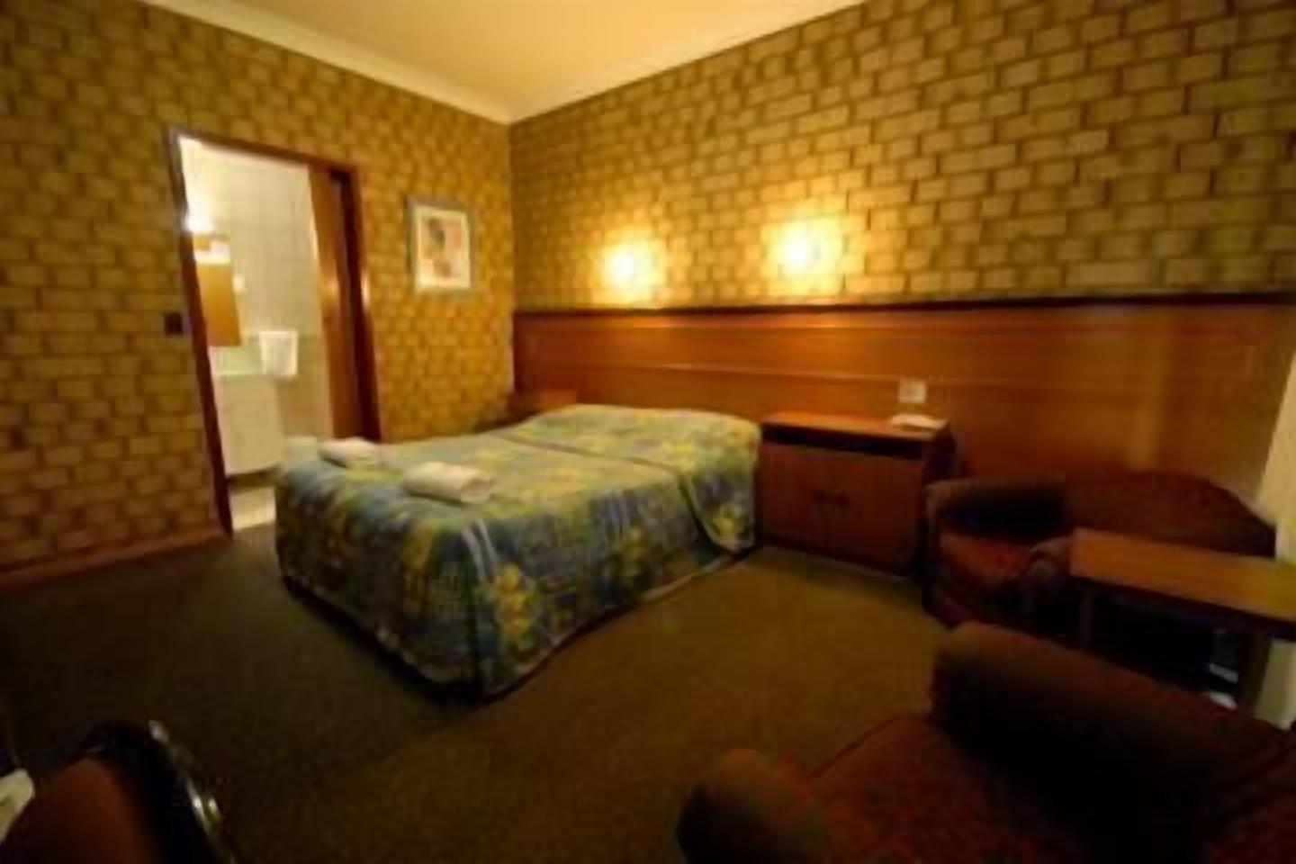 Quarto de hotel com cama, escrivaninha, cadeira e cómoda.