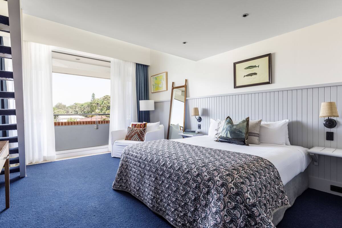 Quarto de hotel com uma cama grande, uma varanda, vista para área verde e um quadro na parede.