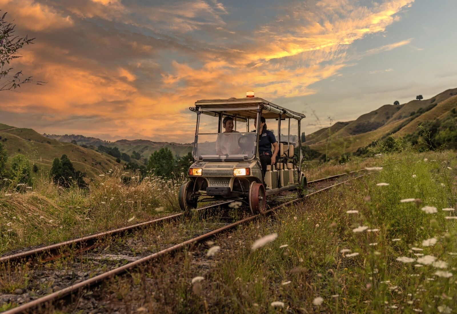 Um trem sobre trilhos em uma paisagem rural com colinas e céu ao pôr do sol.