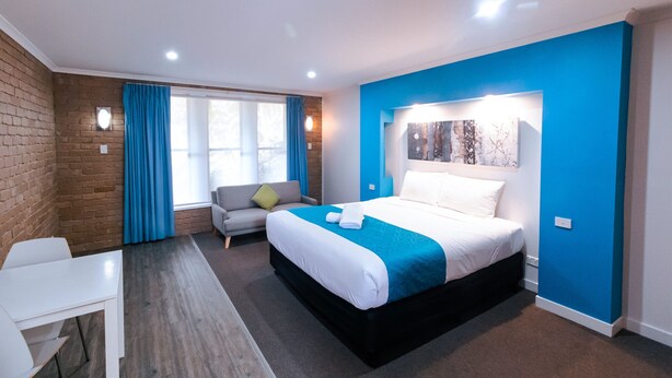 Quarto de hotel moderno com uma cama grande, área de estar com sofá e uma escrivaninha.