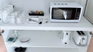 Uma cozinha compacta equipada com micro-ondas, torradeira, chaleira e diversos utensílios e louças.