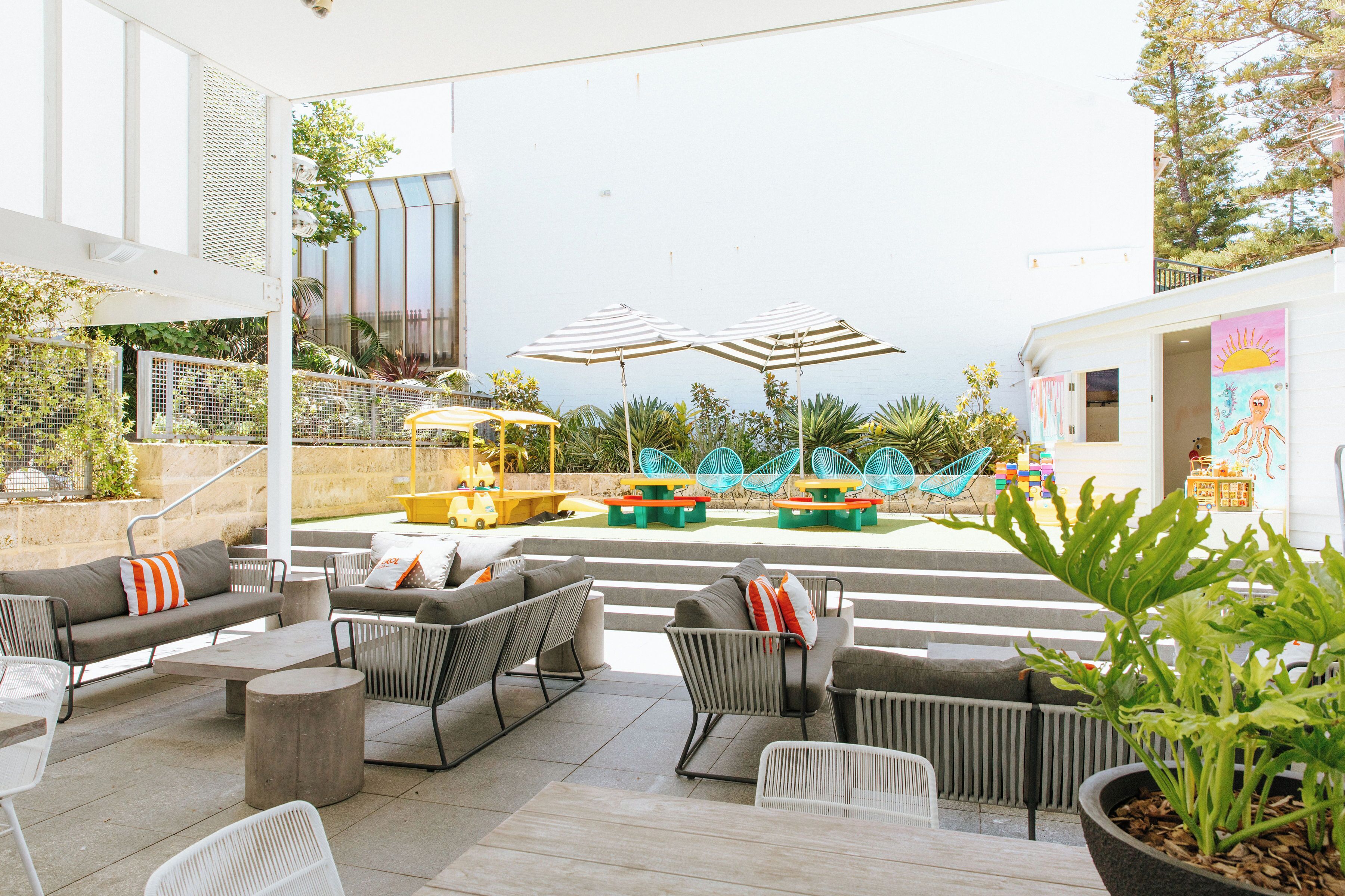 Uma área de estar externa com mobiliário moderno, um espaço de recreação infantil e vista para a paisagem urbana.