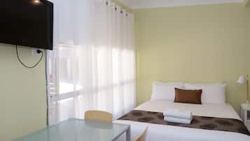 Quarto de hotel com cama, televisão na parede, mesa de vidro e uma cadeira.