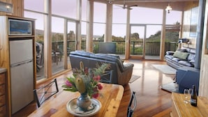 Uma sala de estar ampla com uma mesa de jantar de madeira, um sofá e uma varanda com vista para a paisagem.