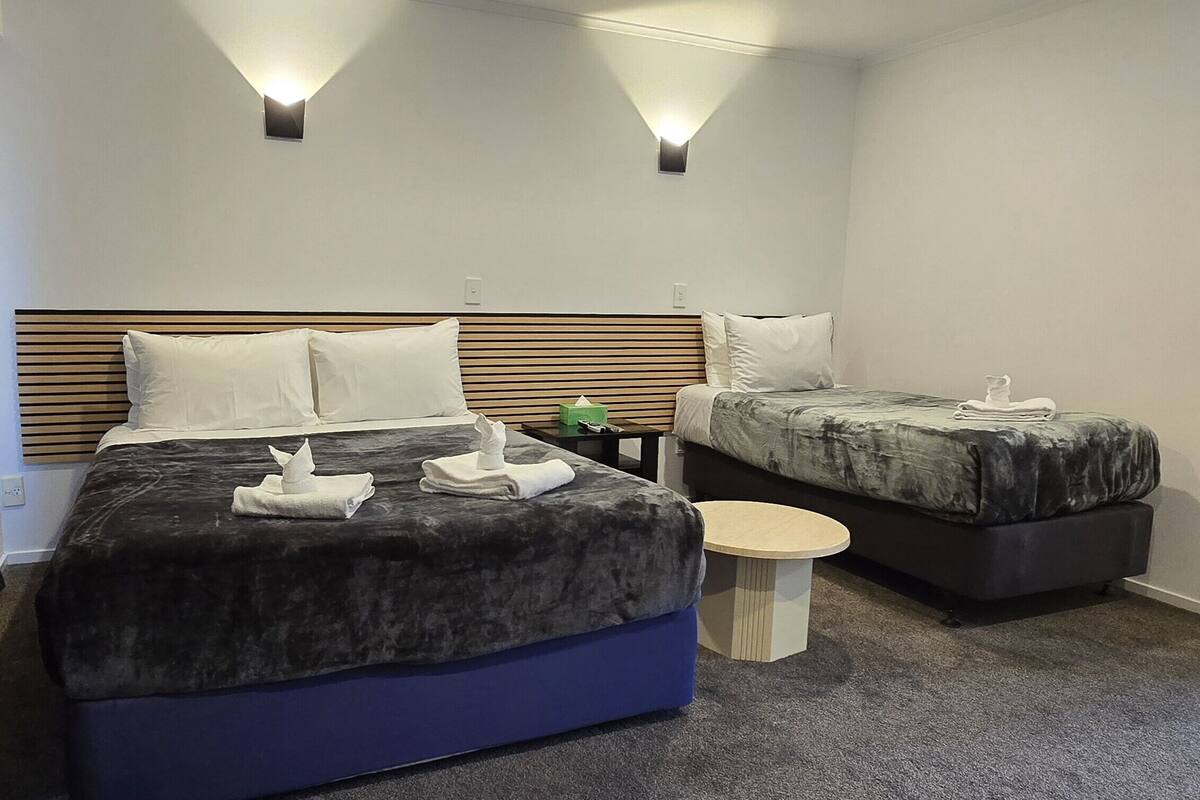 Quarto de hotel com duas camas, cada uma com cabeceira, uma mesa redonda pequena e duas luzes fixadas na parede.