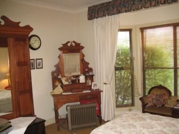 Quarto com uma cama grande, cômoda, espelho e janela com persianas.