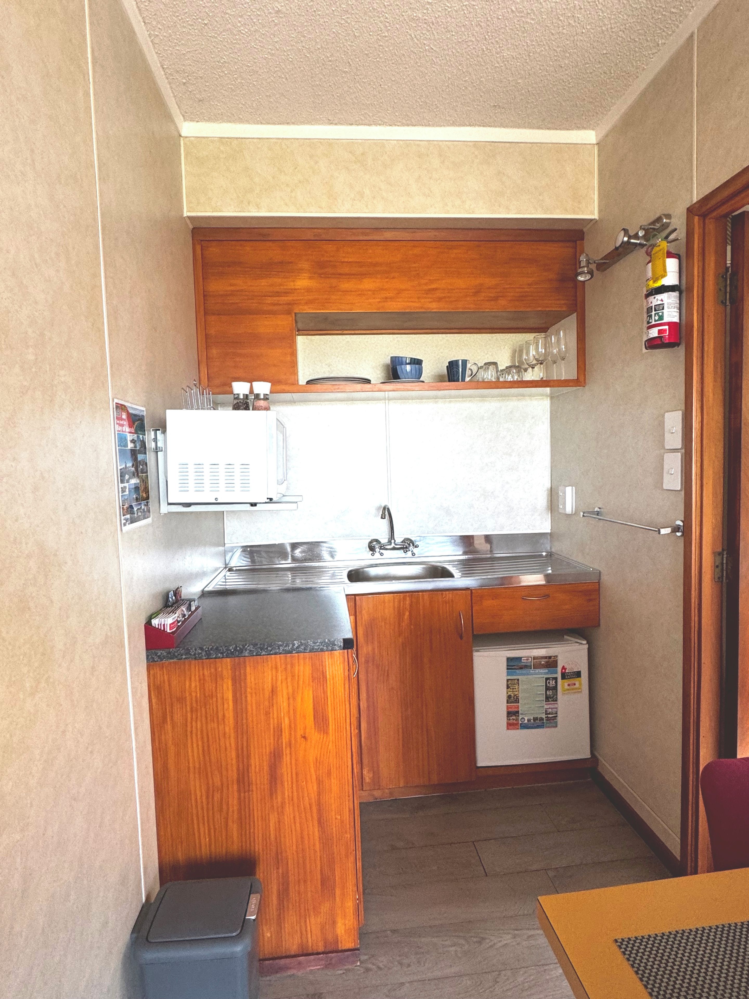 Cozinha compacta com armários de madeira, pia e pequena geladeira.
