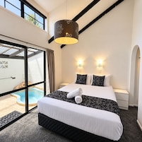 Quarto de hotel com uma cama grande, duas luminárias de cabeceira, janela com vista para uma piscina e um lustre.