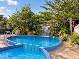 Piscina com cascata, cercada por vegetação exuberante e um boi de salvamento.