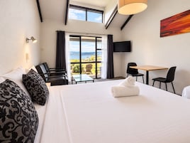 Quarto de hotel com cama, escrivaninha, poltrona, televisão e vista para o exterior.