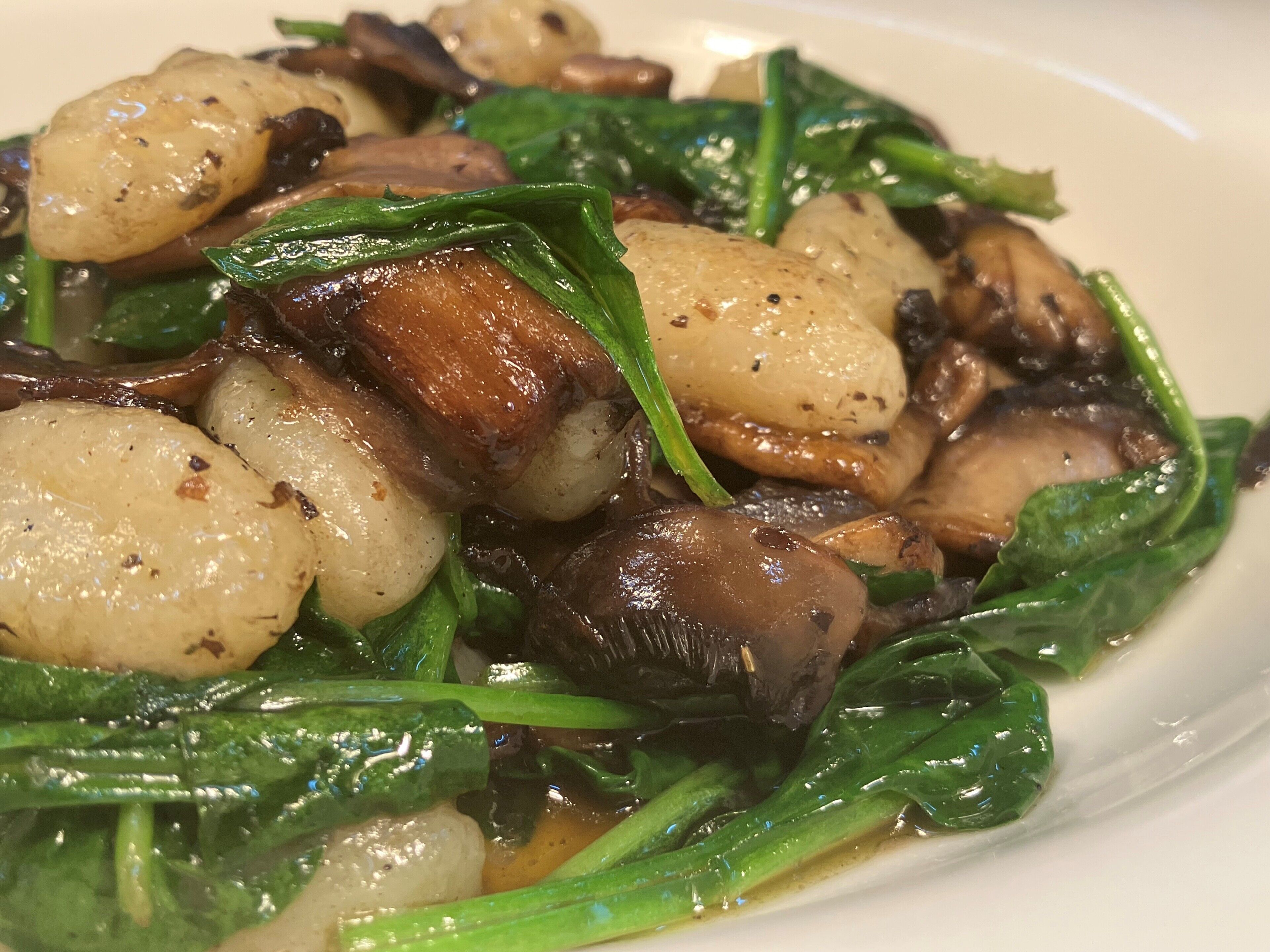 Close-up de um prato com cogumelos, batatas e folhas verdes.