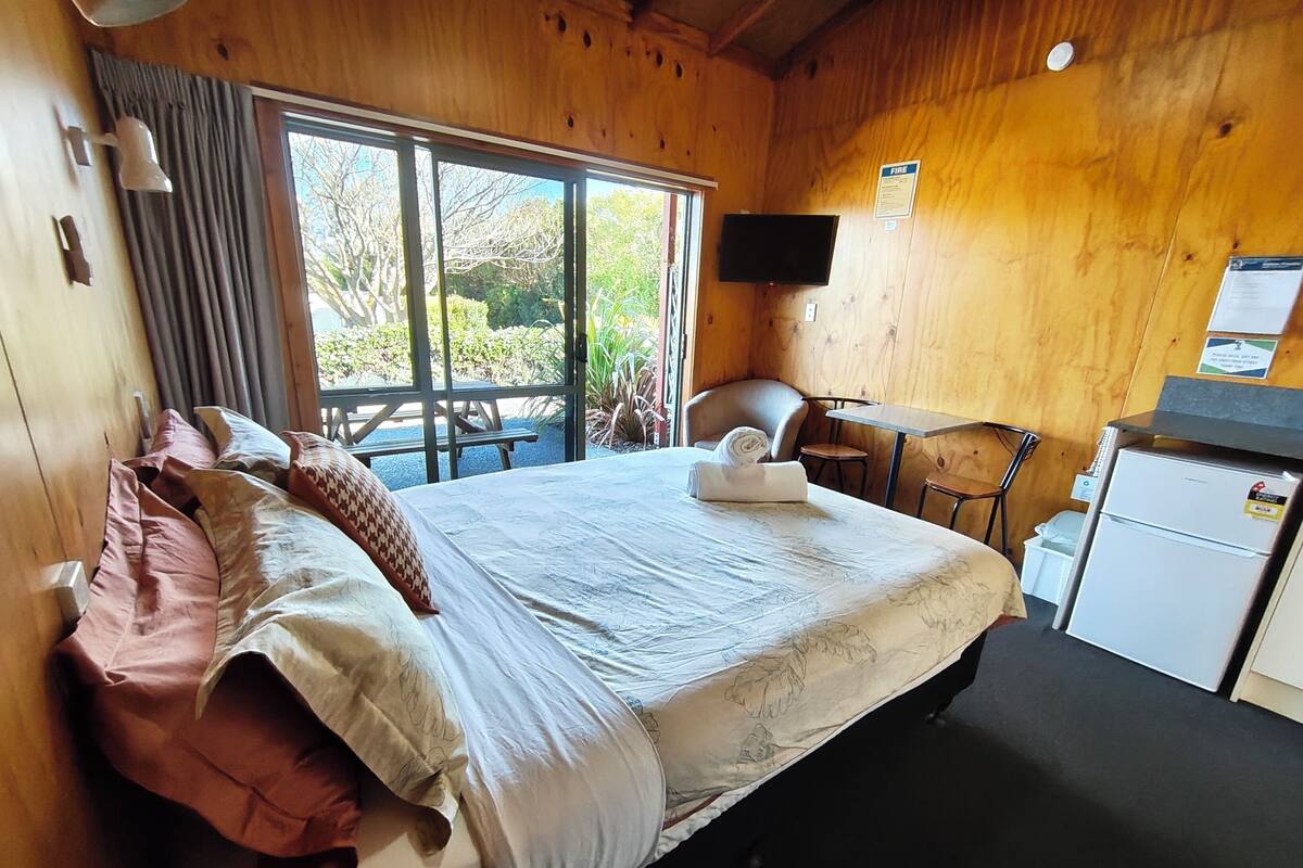 Quarto de cabana de madeira com cama, escrivaninha, cadeira e televisão.