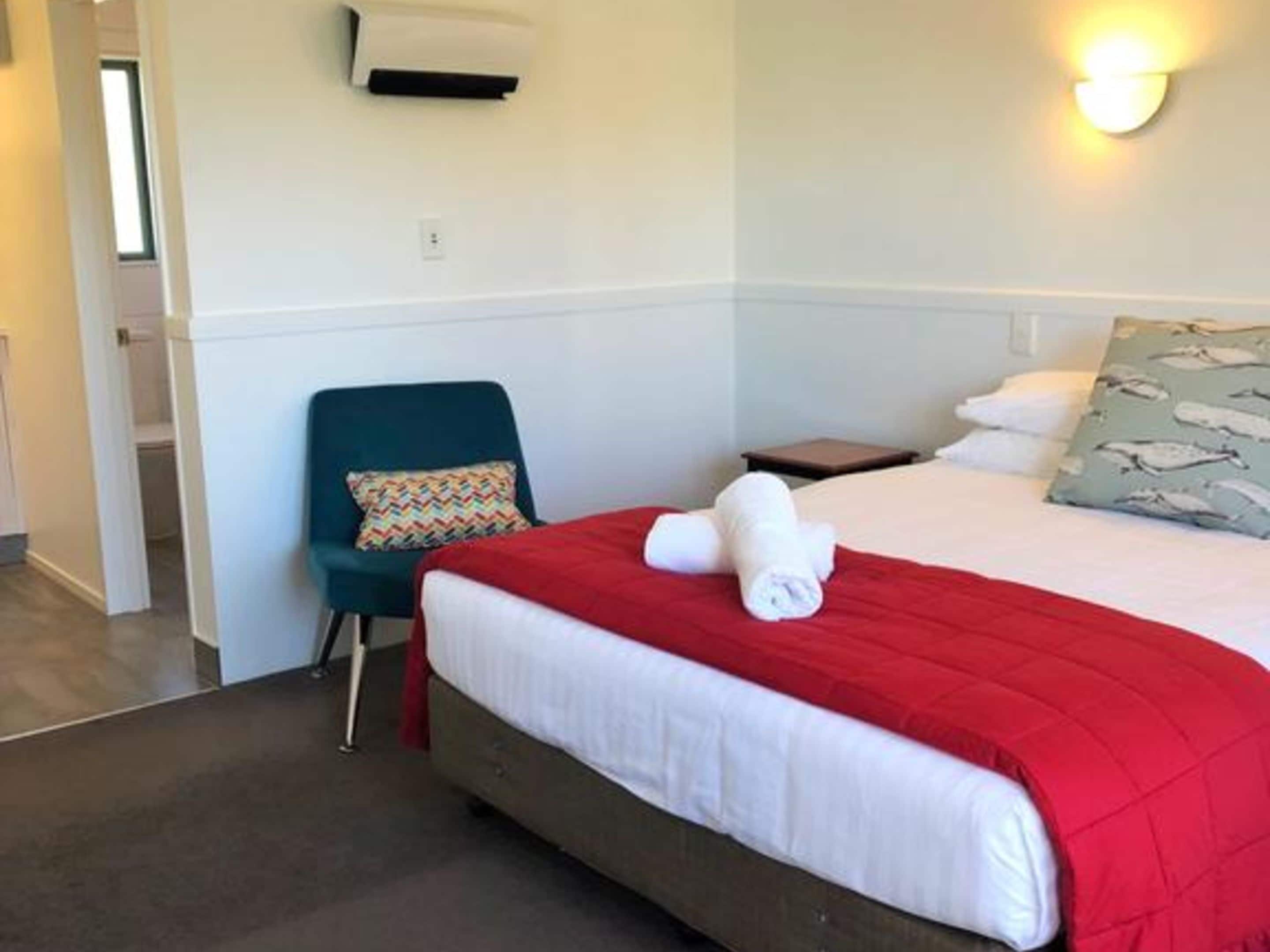 Quarto de hotel com uma cama, uma cadeira, uma mesa de cabeceira e uma luminária na parede.