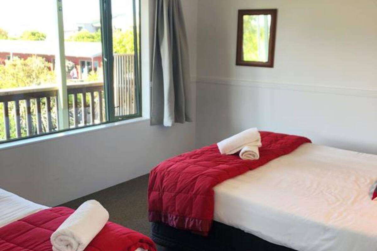 Quarto de hotel com duas camas, uma janela grande com vista para o exterior e um pequeno porta-retrato na parede.