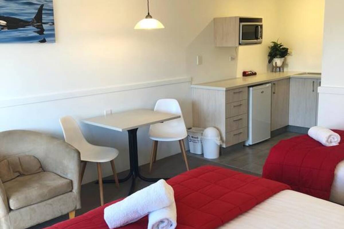 Quarto de hotel compacto com cama, pequena mesa, cadeira, sofá, micro-ondas e pia.