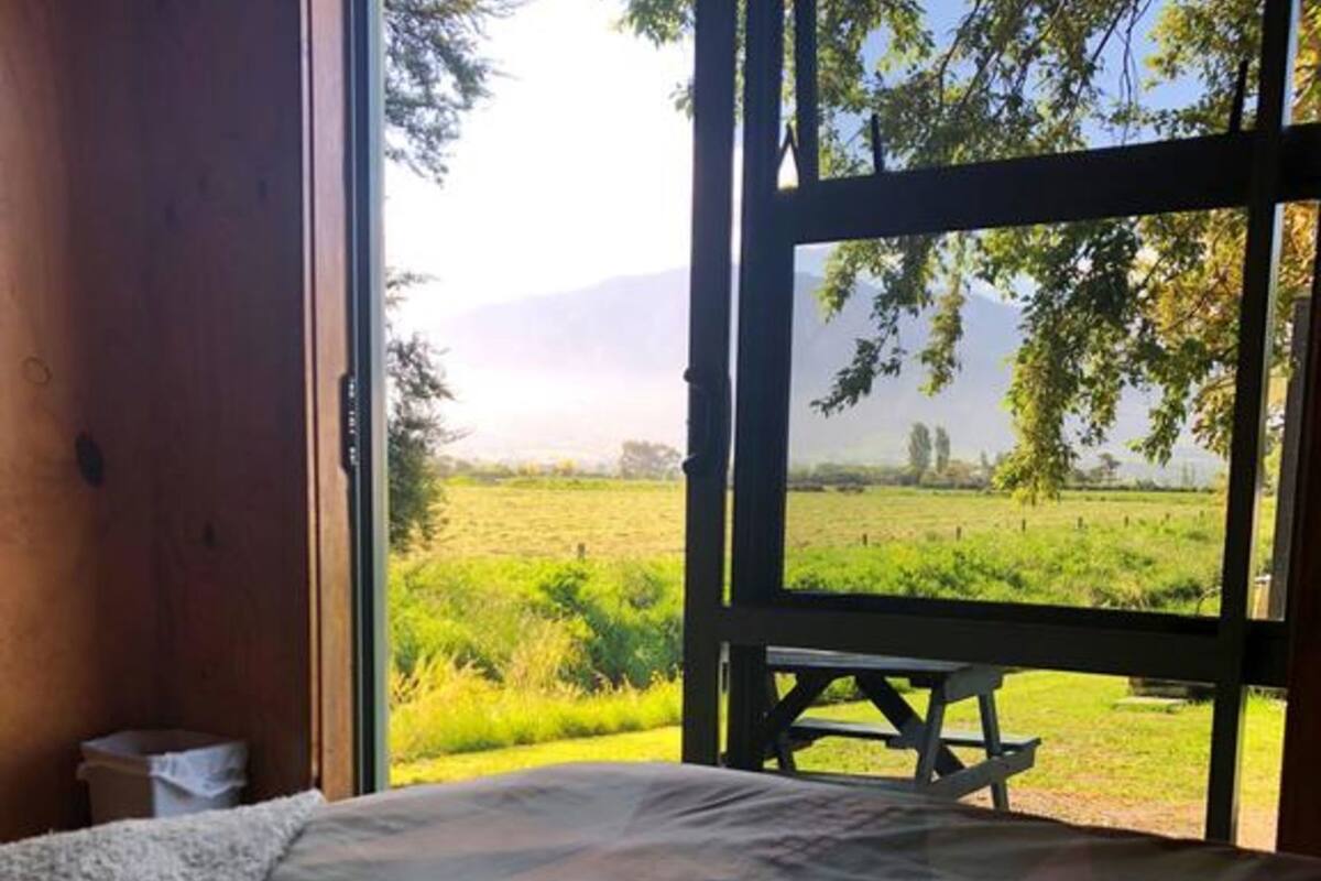 Um quarto com cama, janela e vista para um campo verde.