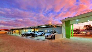 Um posto de combustíveis com várias bombas de gasolina, uma área de estacionamento coberta e céu claro.