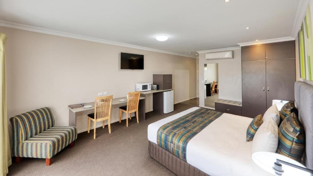 Quarto de hotel com cama, escrivaninha, cadeira, televisão e guarda-roupa.