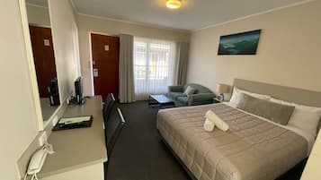 Quarto de hotel com uma cama, uma escrivaninha com telefone, uma cadeira, uma mesinha e uma janela com cortinas.