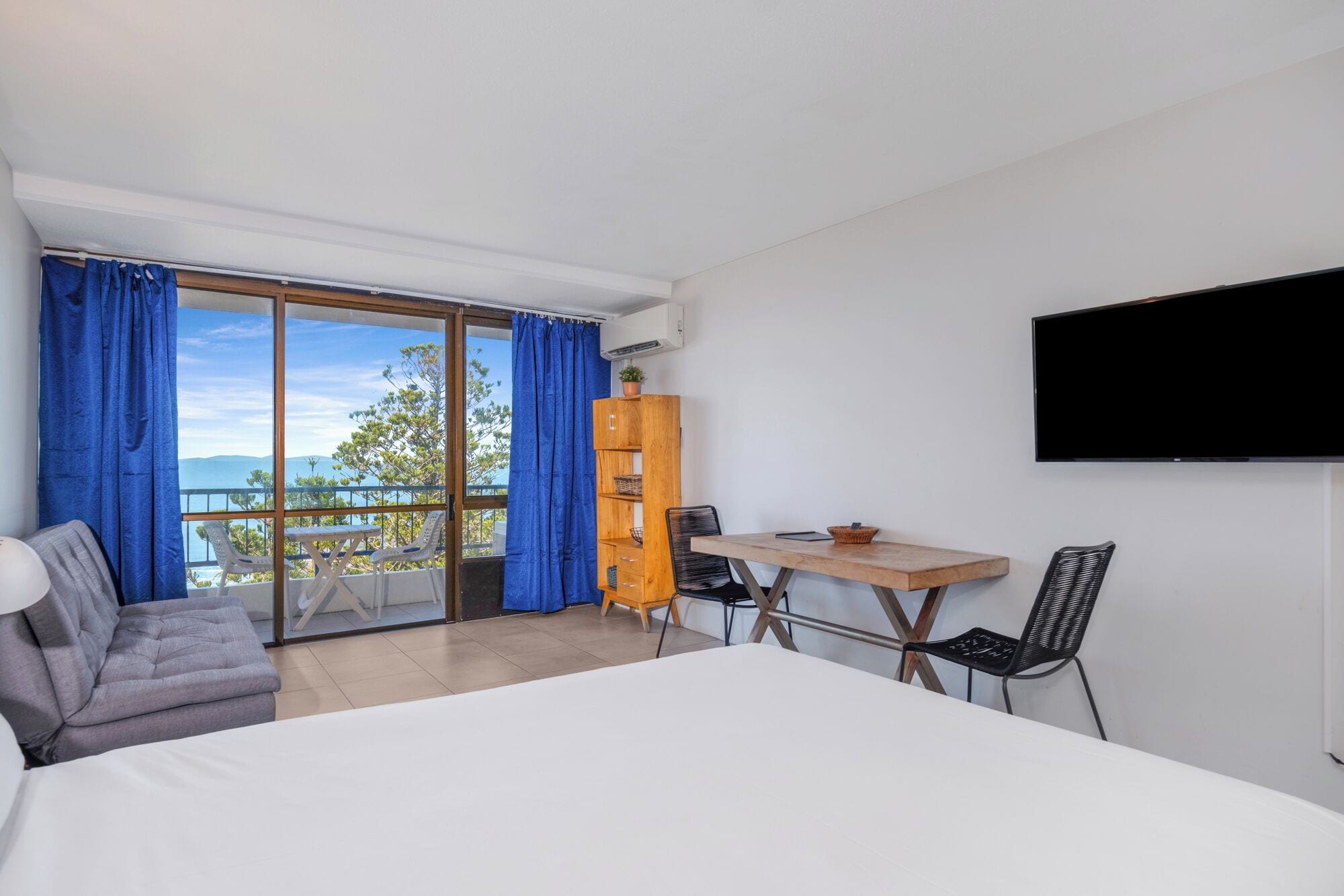 Quarto de hotel com uma cama, uma escrivaninha, uma cadeira, uma televisão e vista para o mar.