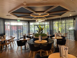 Interior de restaurante moderno com mesas redondas, cadeiras pretas e uma planta central.