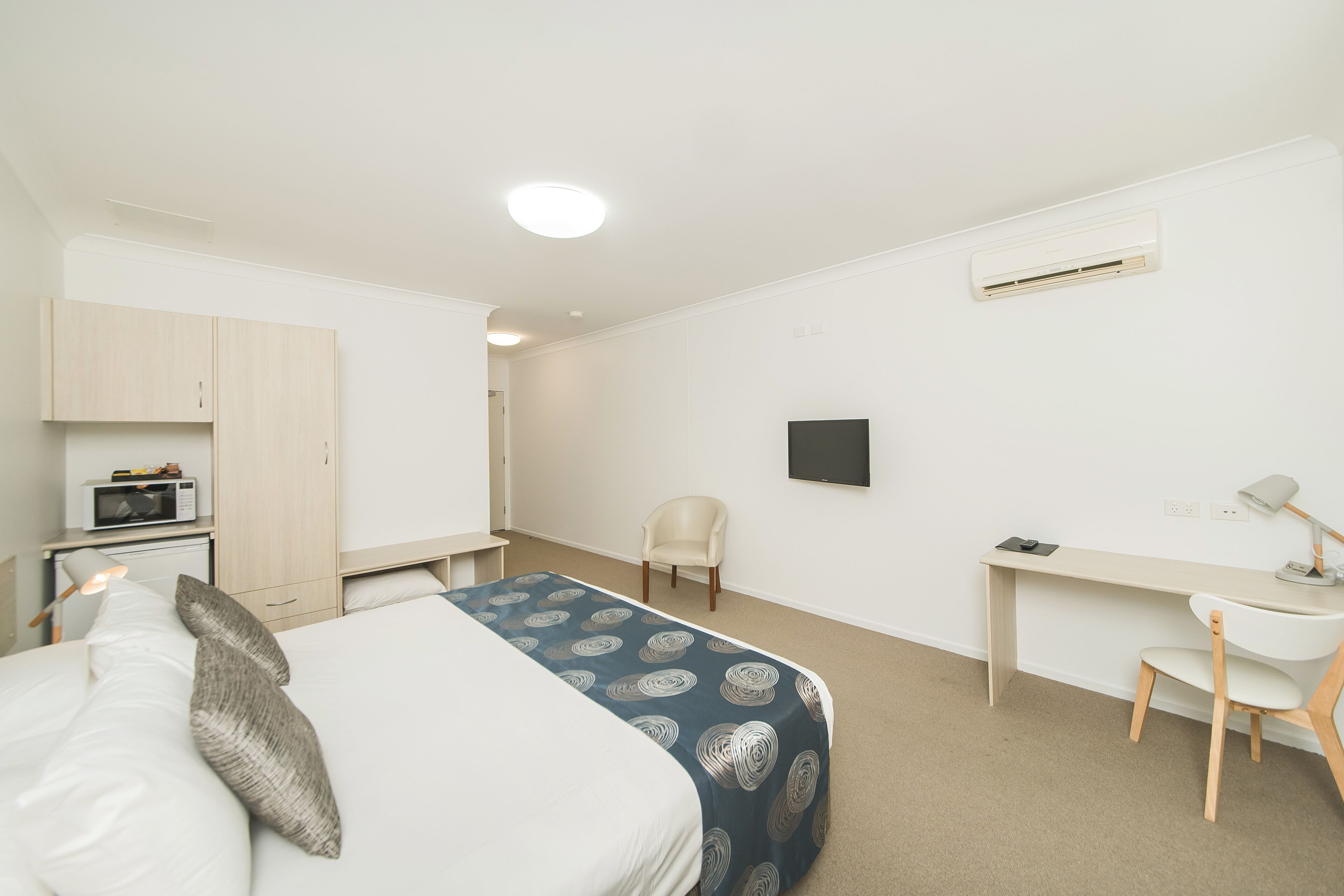 Quarto de hotel com cama, escrivaninha, cadeira, micro-ondas e televisão.