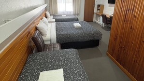 Quarto de hotel com três camas, um guarda-roupa de madeira, uma escrivaninha e uma televisão.