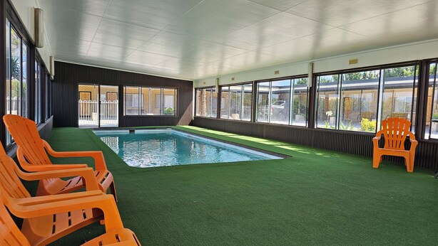 Piscina interna com grama sintética, janelas amplas e cadeiras laranja.