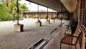 Um motel com área de estacionamento coberta, espaço para sentar ao ar livre e entrada por um caminho de cascalho.